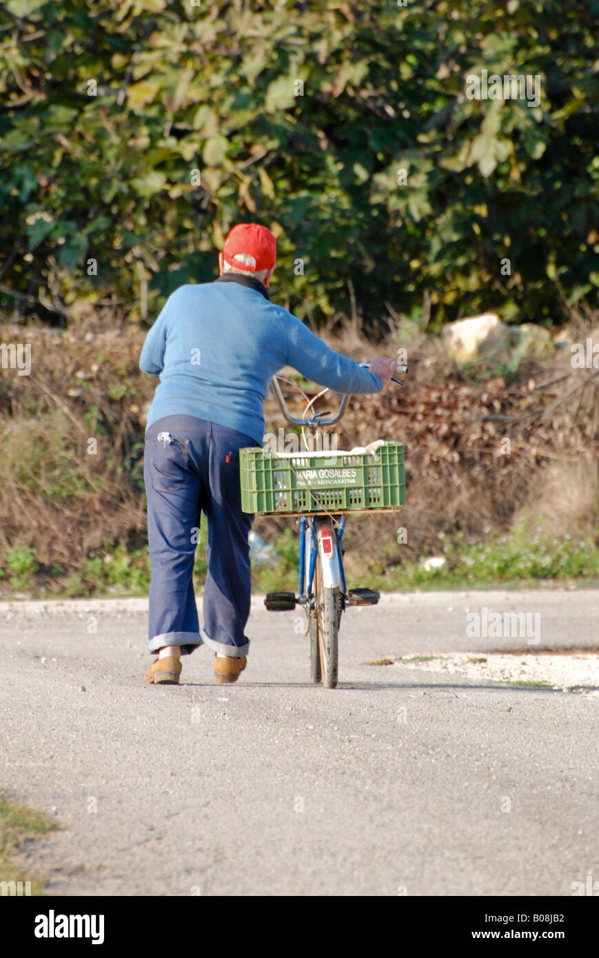 Elderly man pushing bicycle with basket along road Stock Photo - Alamy
