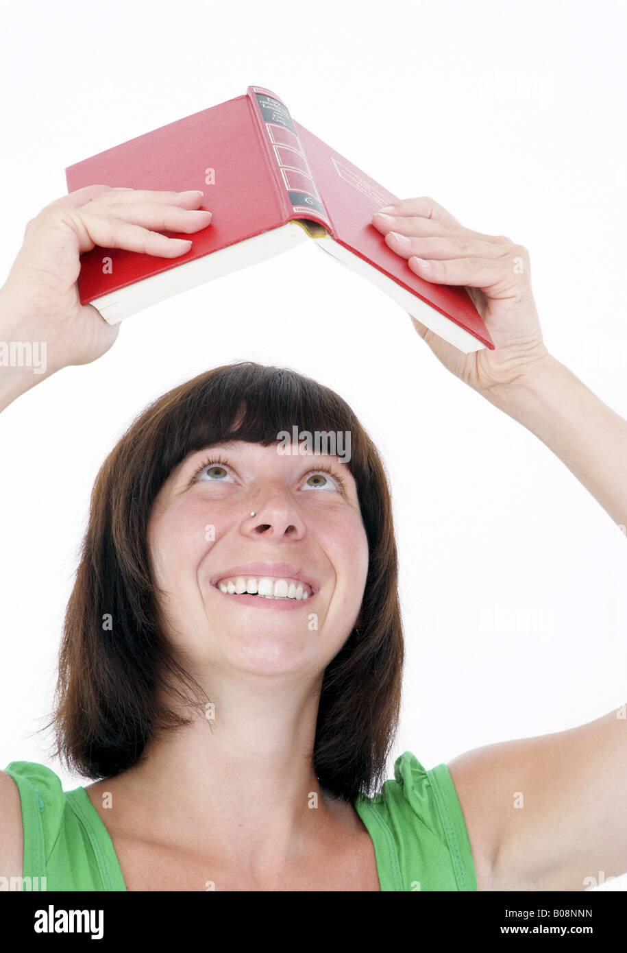 brown-haired woman in a green t-shirt, holding a book over her head ...