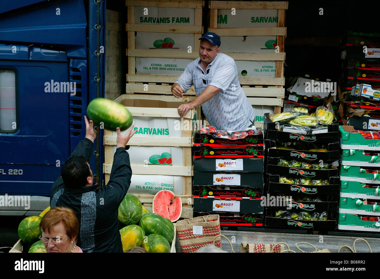 Fruit vendor unloading crates from a truck, tossing a watermelon ...