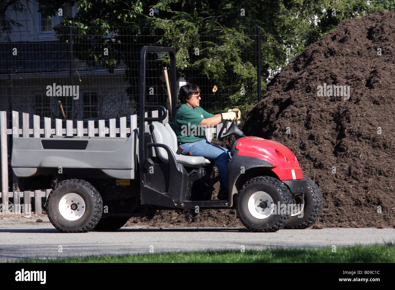 A garden worker driving a utility vehicle with a cart in front of a ...