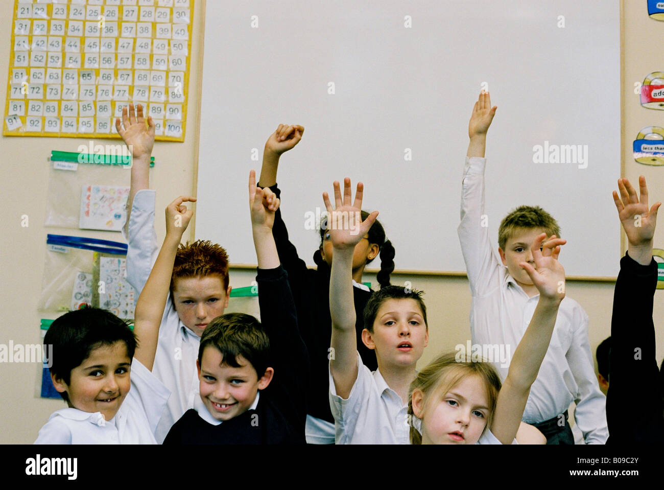 Primary school pupils,hands up in class Stock Photo - Alamy