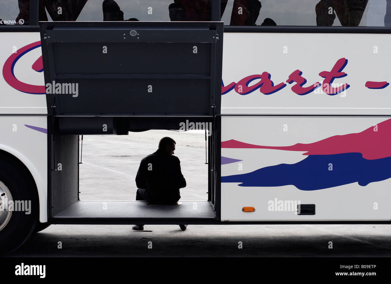 Man sitting in open empty luggage compartment of French tourist bus ...
