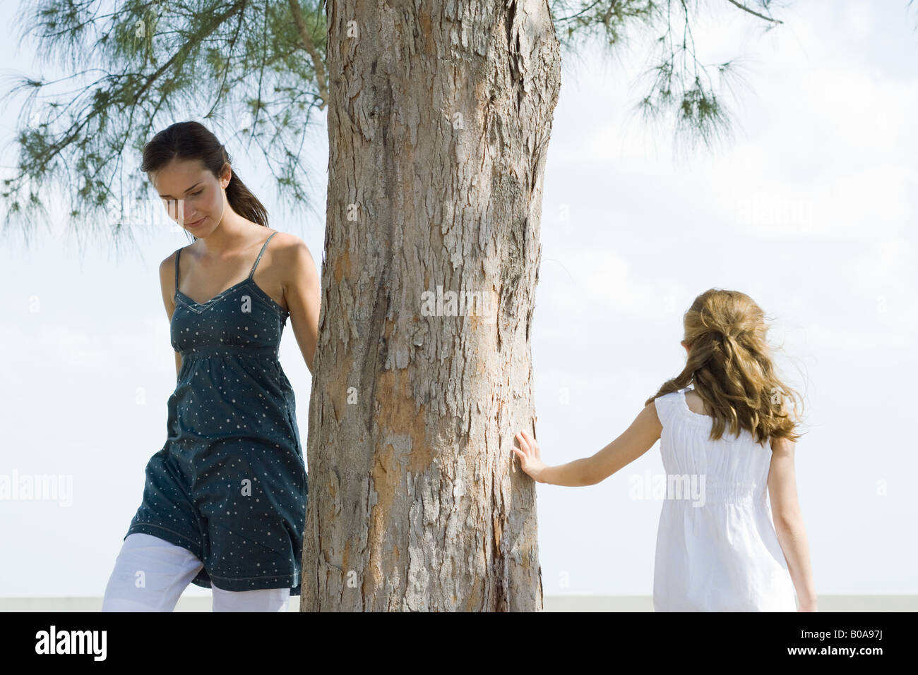 Two sisters walking around tree trunk, little girl touching tree with ...