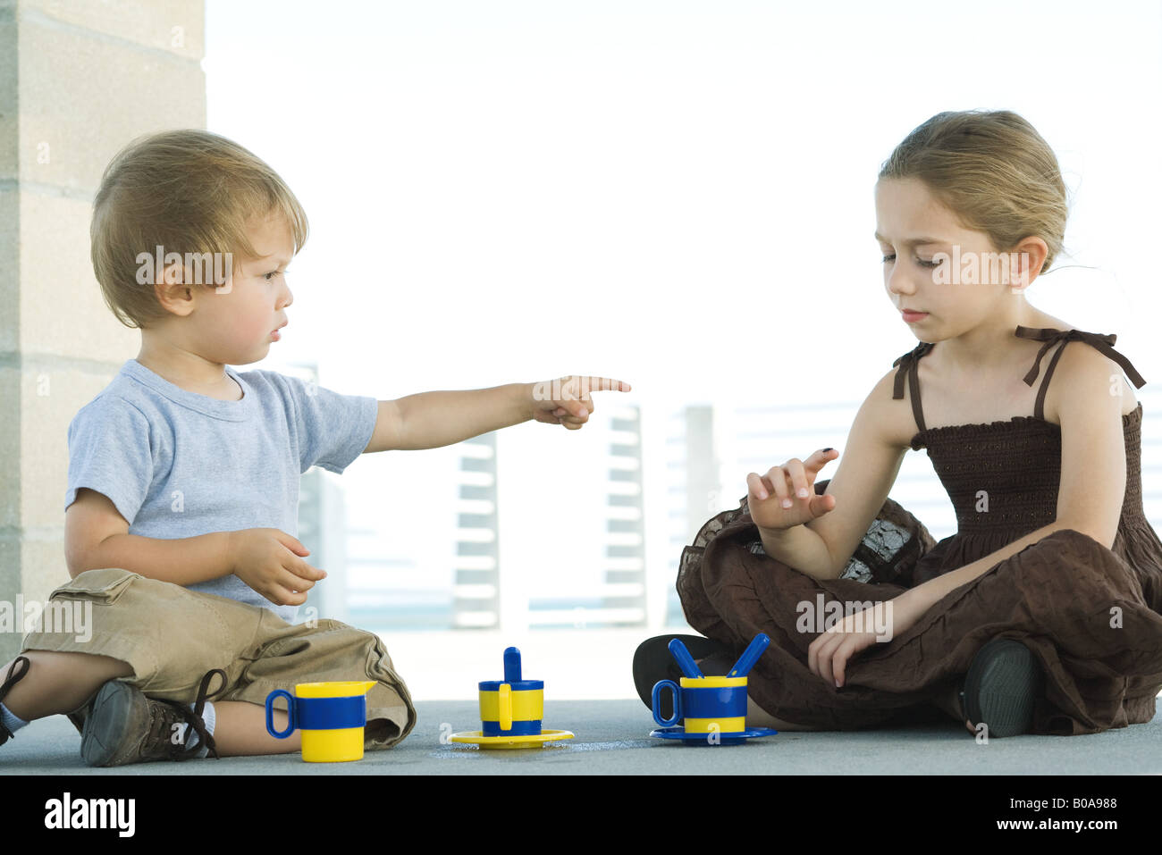 Siblings sitting on the ground together, brother pointing a sister ...