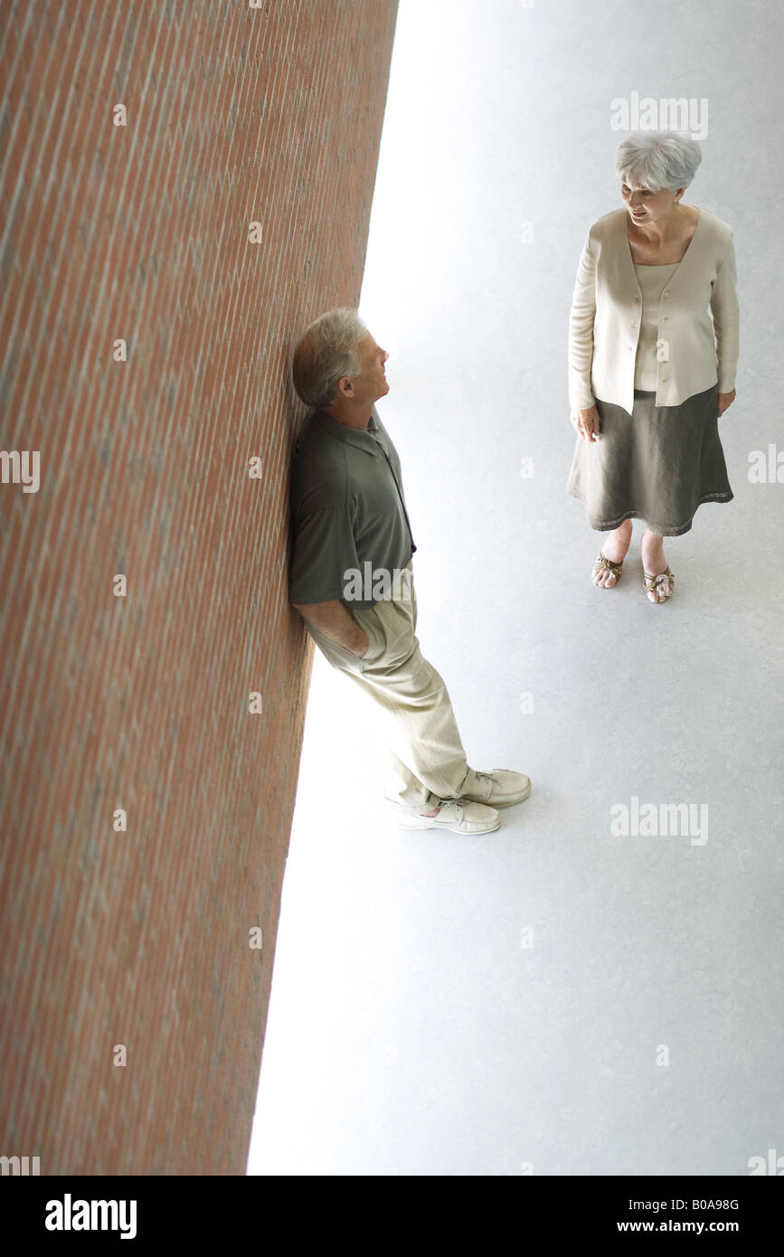 Couple talking together, man leaning against wall with hands in pockets ...