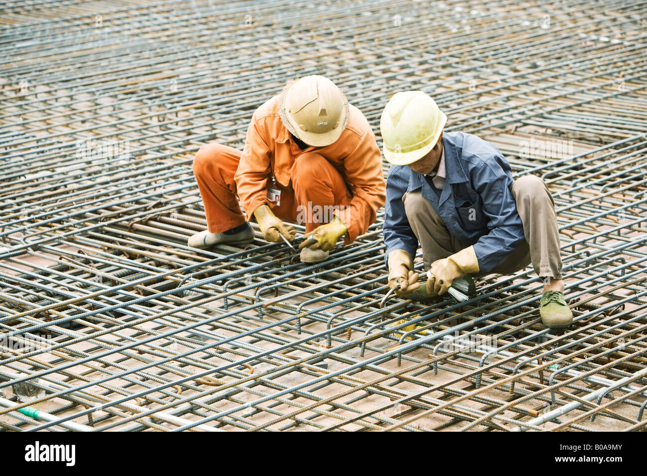 Construction workers crouching on steel framework, both looking down ...