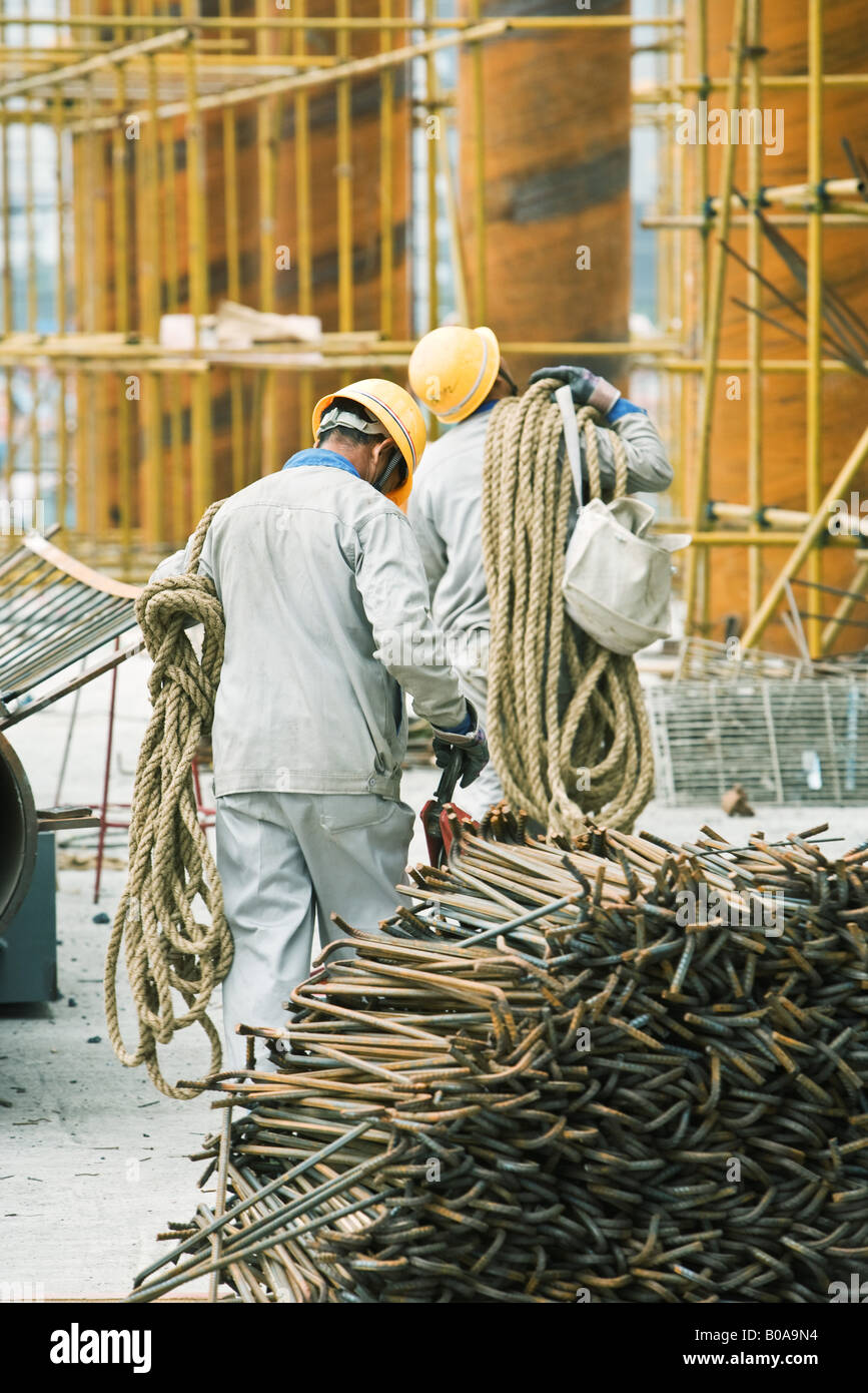 Workers at construction site carrying rope, metal rods stacked in ...