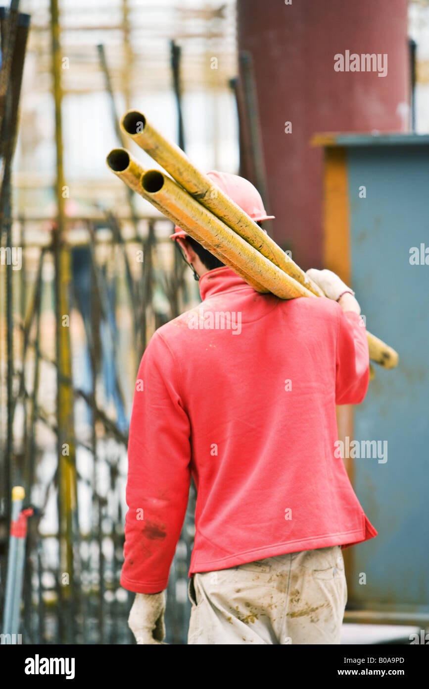 Worker at construction site carrying metal rods on shoulder Stock Photo ...