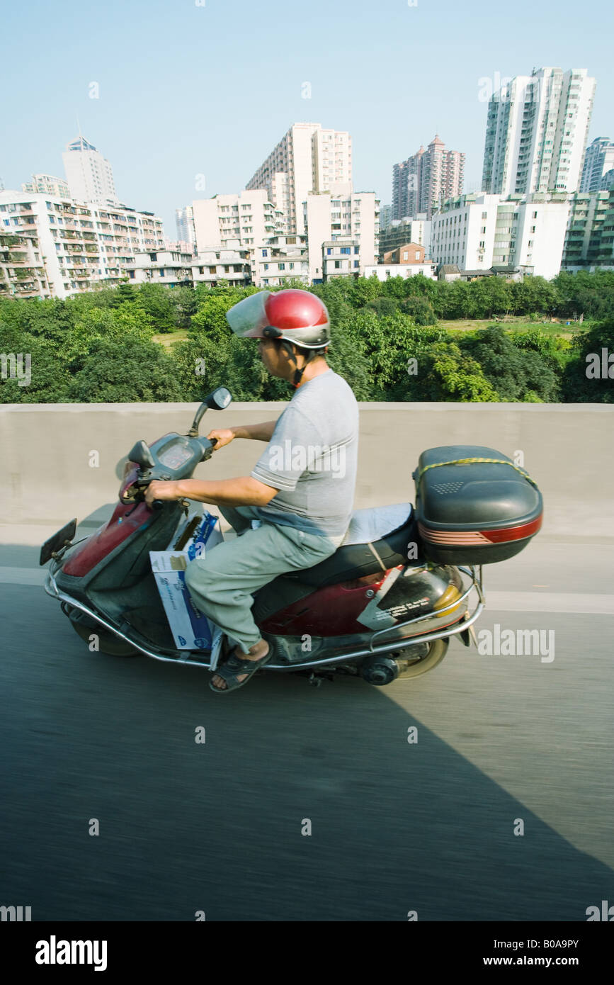 China, Guangzhou, man riding motor scooter, high-rise buildings in ...