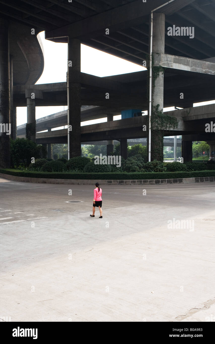 China, Guangzhou, female pedestrian walking under bridge, rear view ...