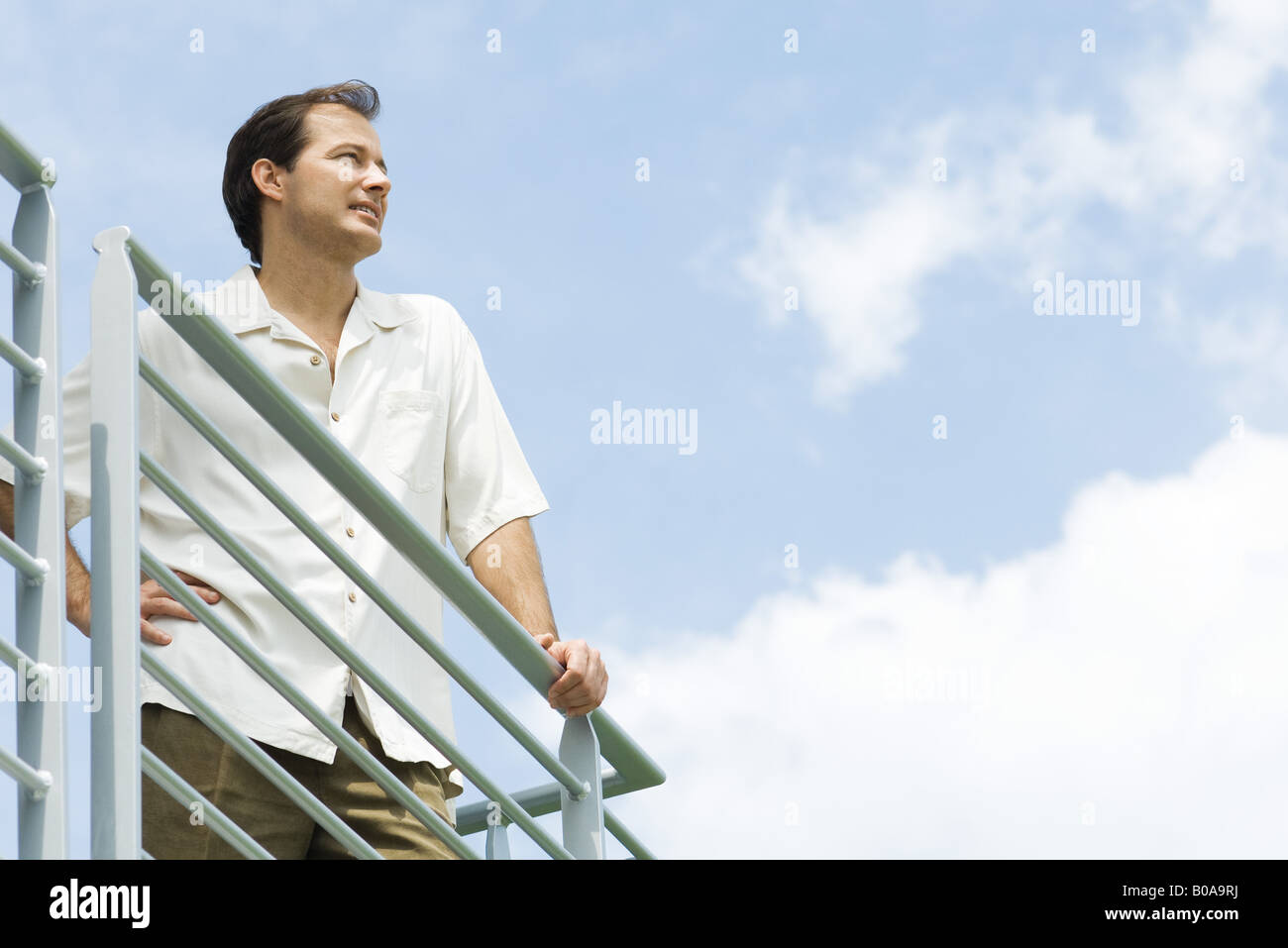 Man leaning against railing, looking into distance, low angle view ...