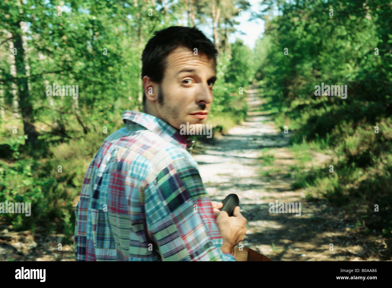 Man walking on path in woods, looking over shoulder at camera, close-up ...