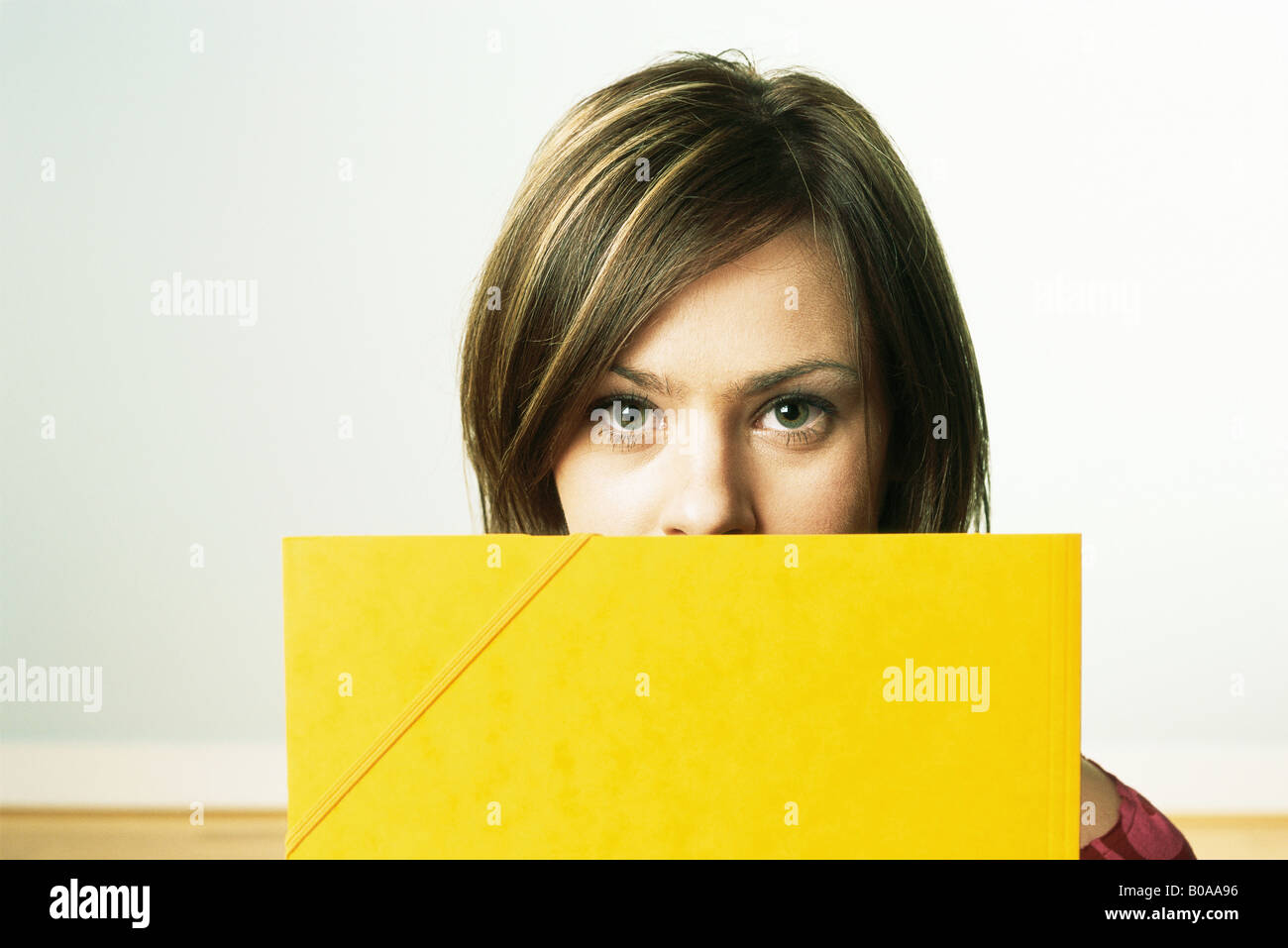 Female holding folder in front of face, looking at camera Stock Photo ...