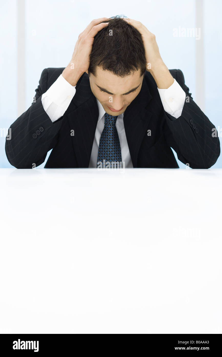 Businessman sitting, holding head, looking down Stock Photo - Alamy