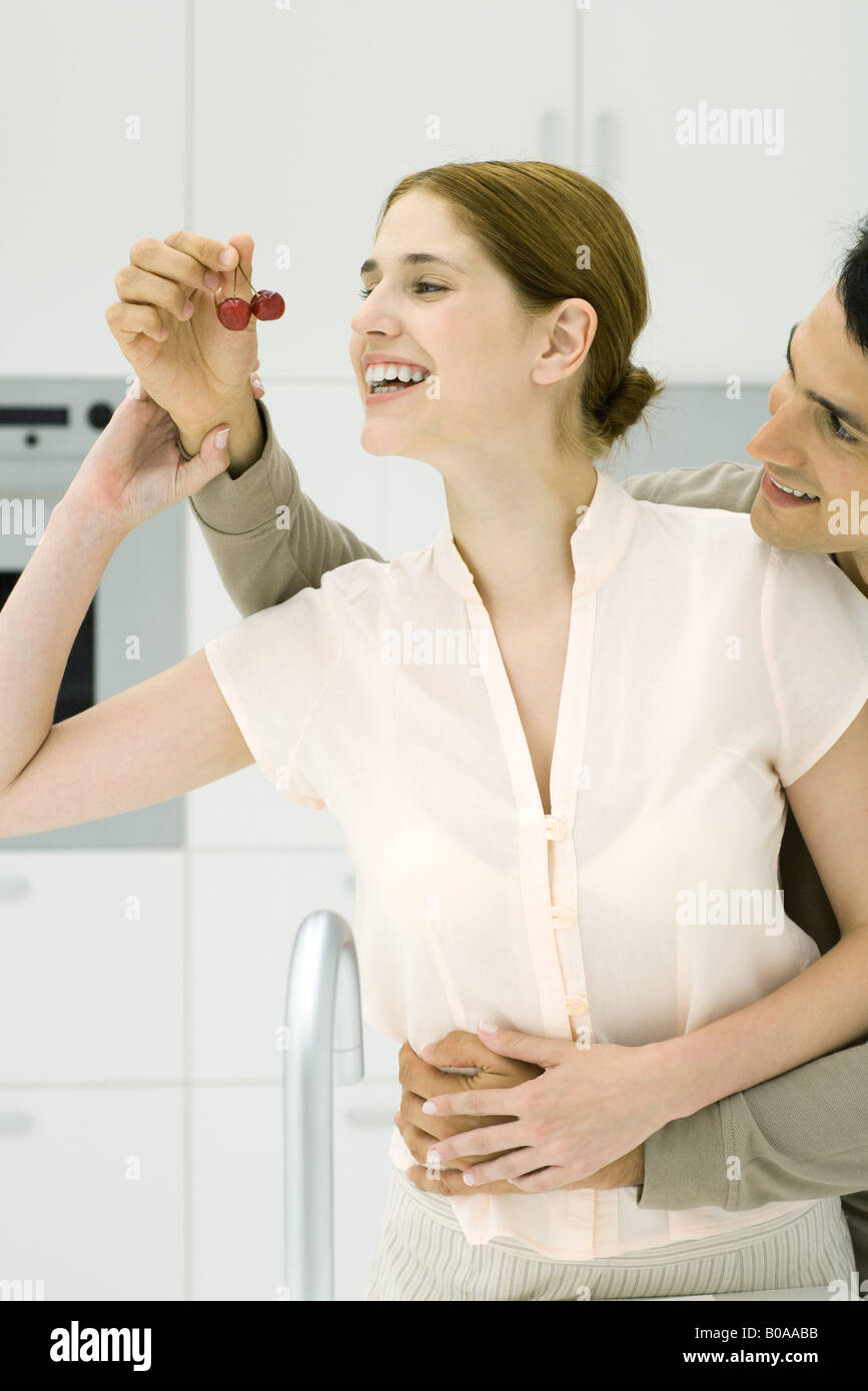 Young couple in kitchen, man feeding woman cherries Stock Photo - Alamy