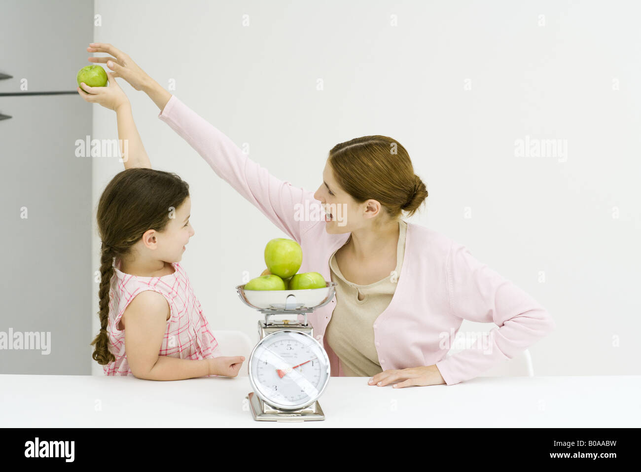 Woman and girl, girl holding up apple, woman reaching for it Stock ...