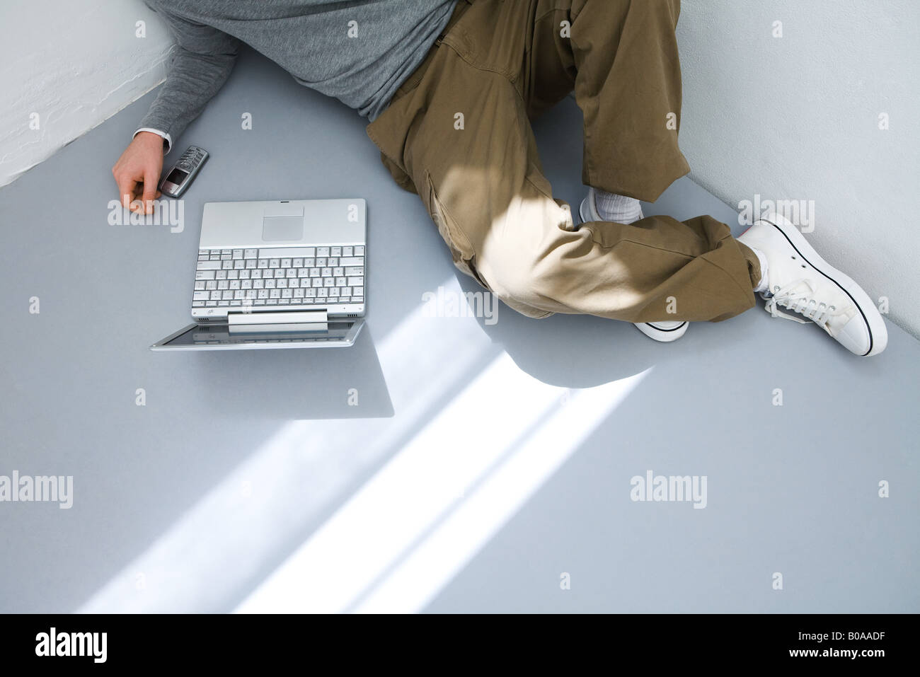 Young man sitting on the ground in front of laptop computer, cropped ...