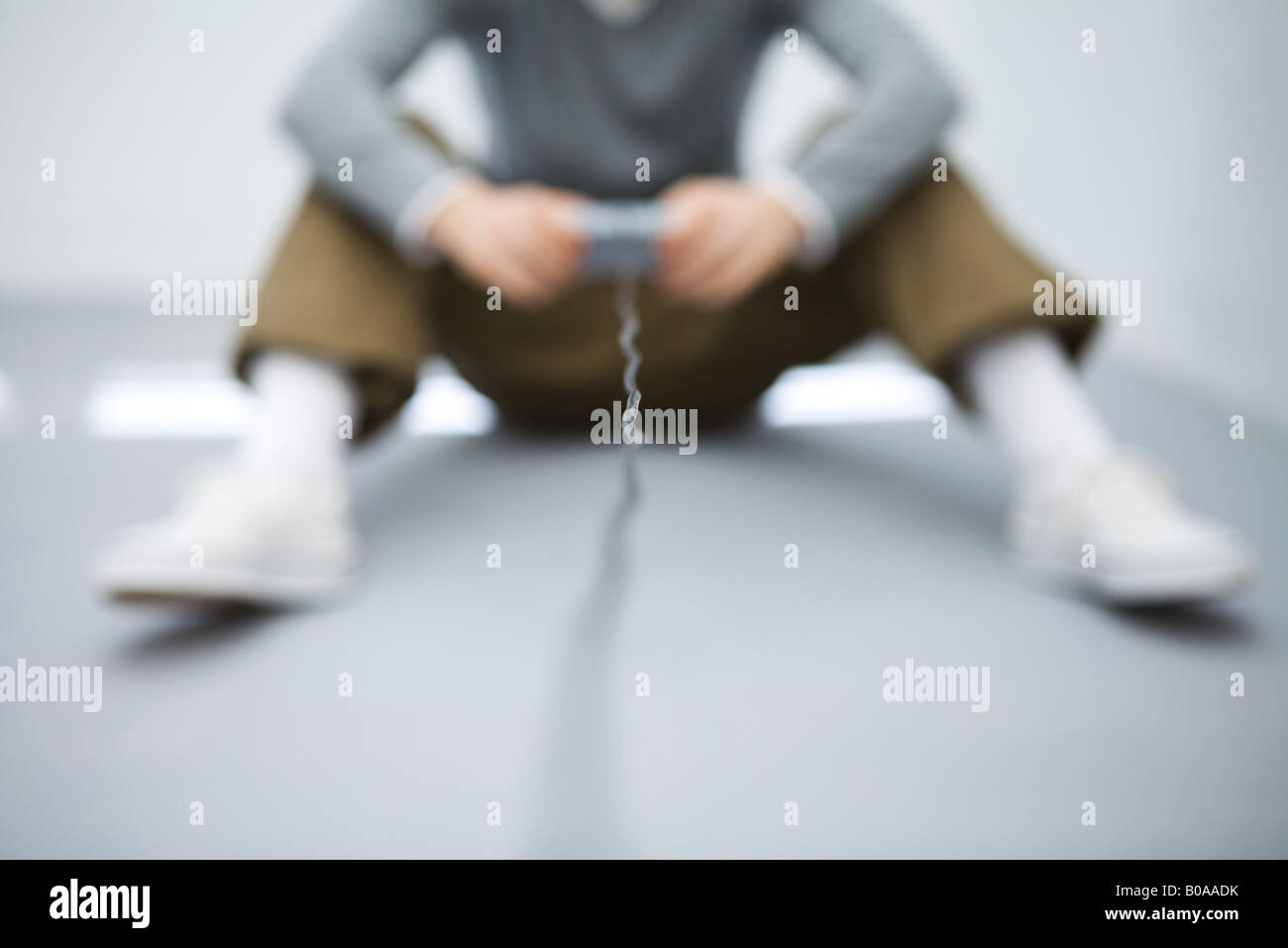 Young man sitting on the ground, holding video game controller, cropped ...