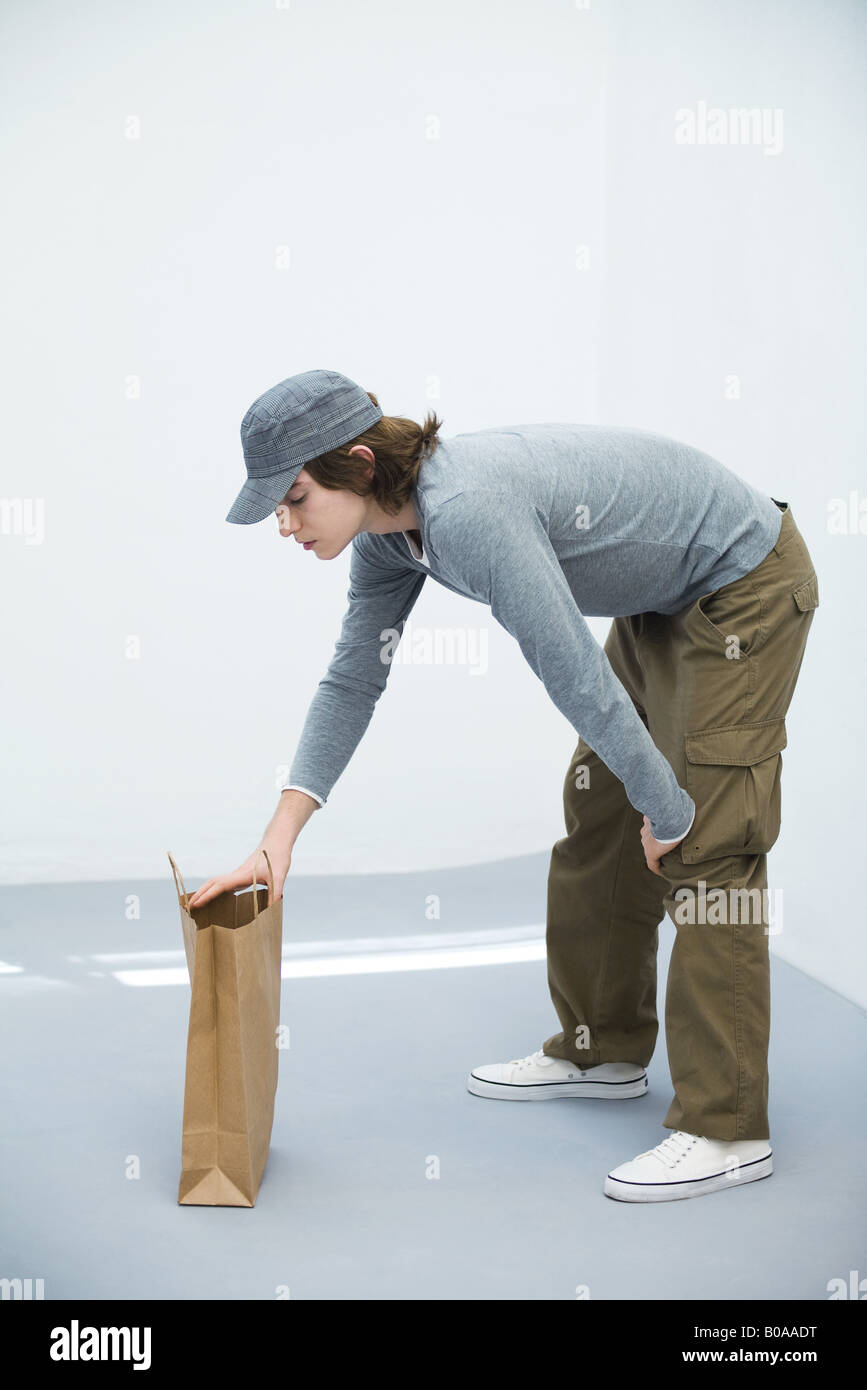 Young man bending over, looking in paper shopping bag, side view Stock ...