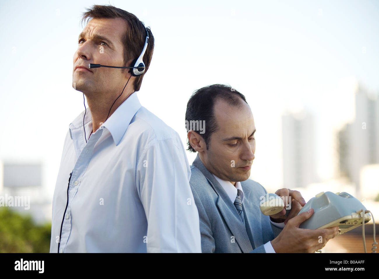 Two men standing back to back, one using headset, the other holding ...