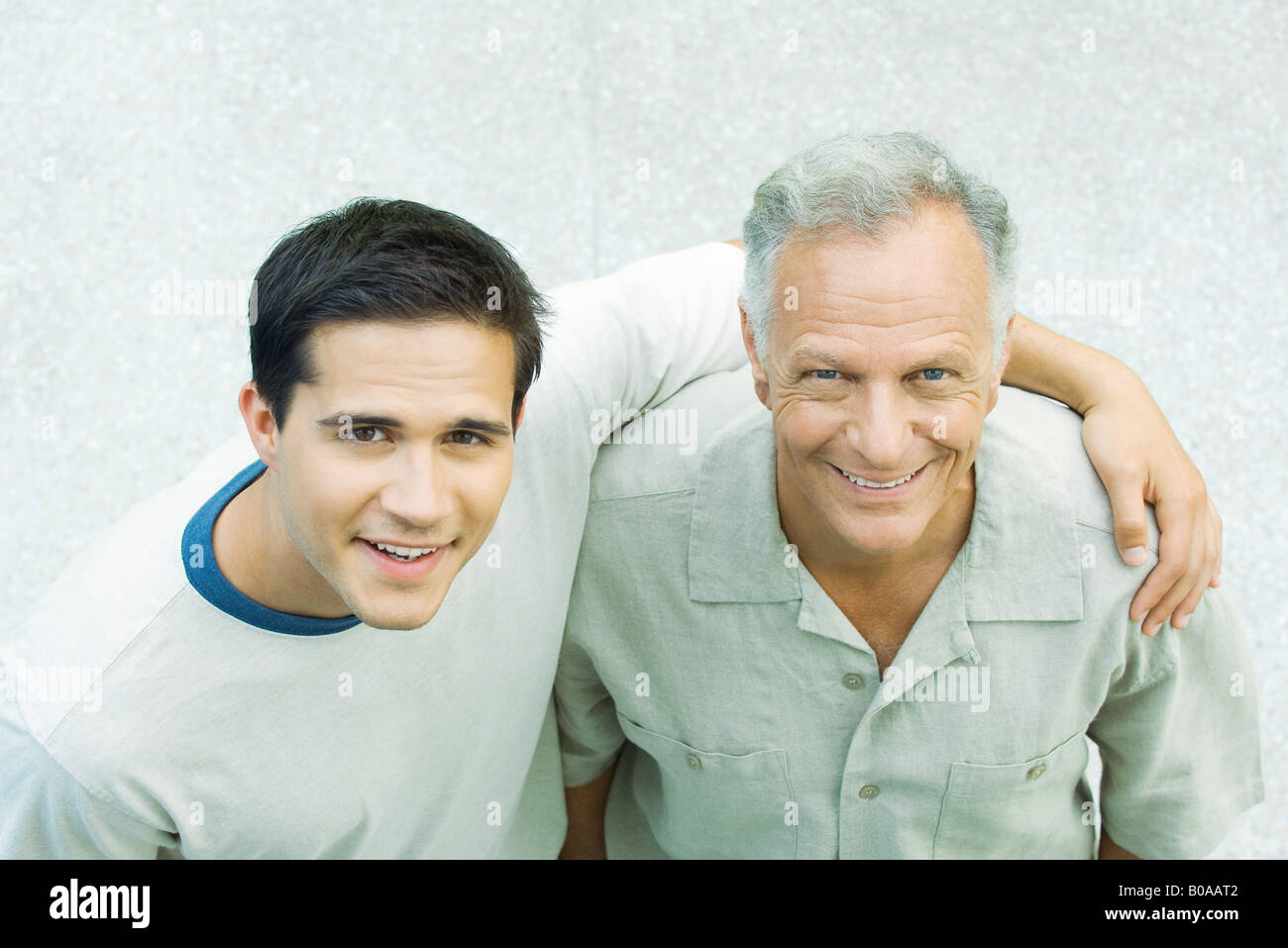 Young man with arm around his father's shoulder, both smiling at camera ...