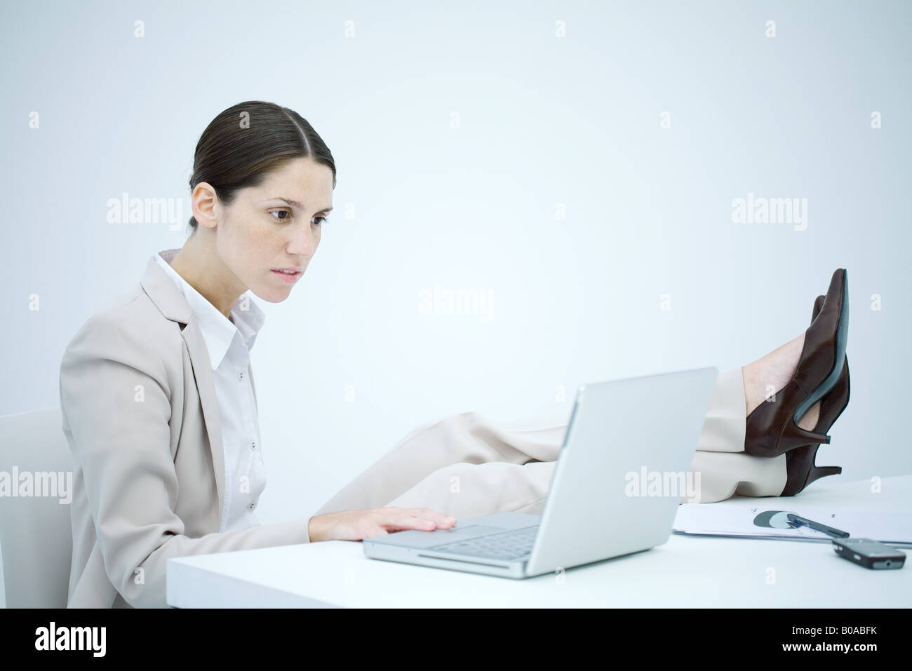 Businesswoman sitting at desk with legs up, using laptop Stock Photo ...