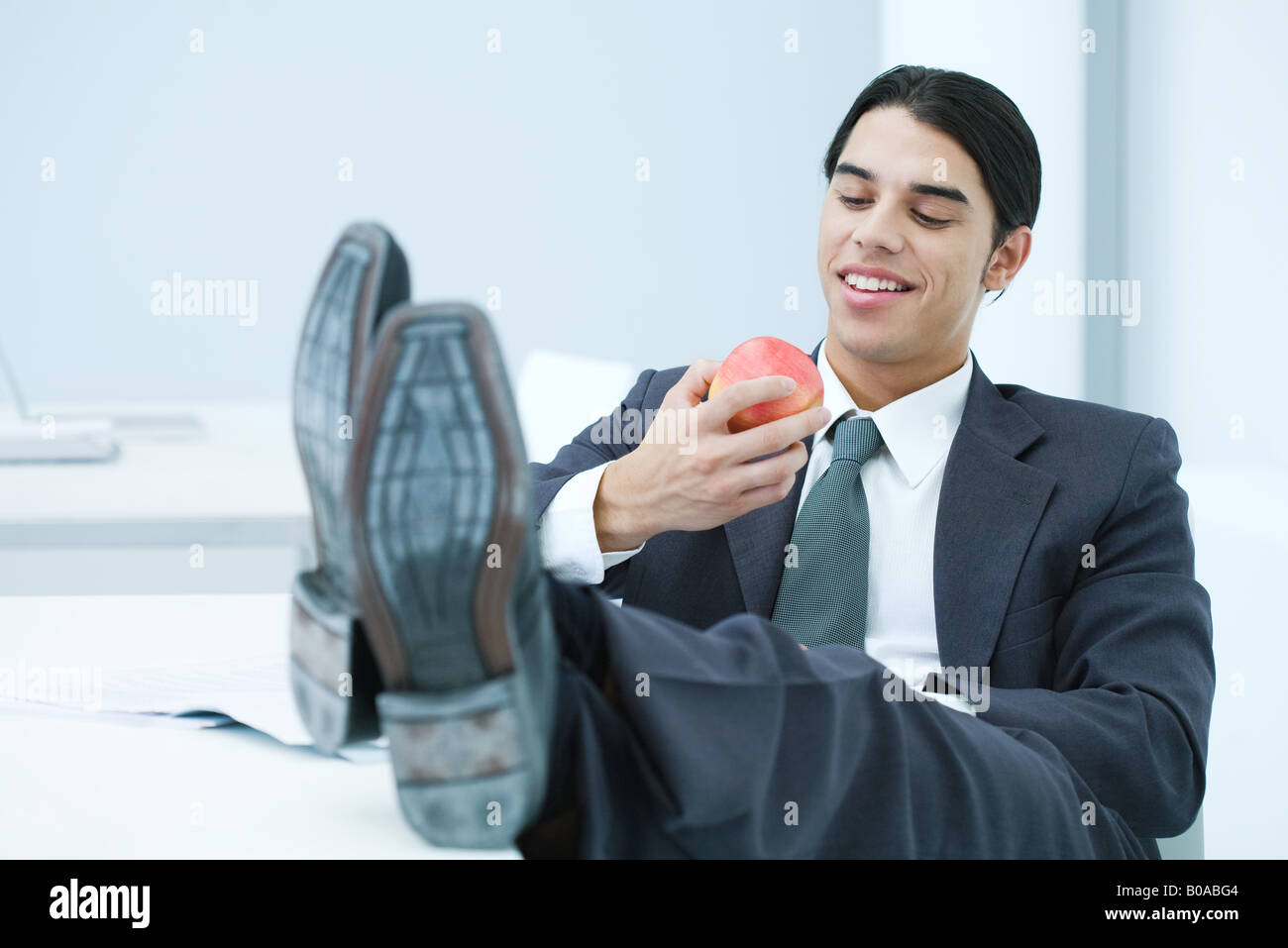 Young businessman sitting at desk with feet up, eating apple Stock ...