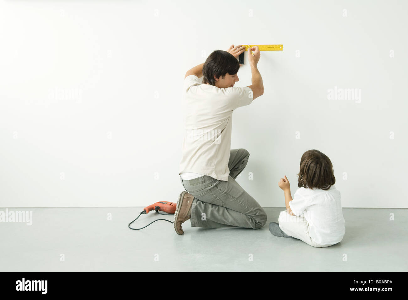 Man measuring wall with a ruler while his son watches, drill on the ...