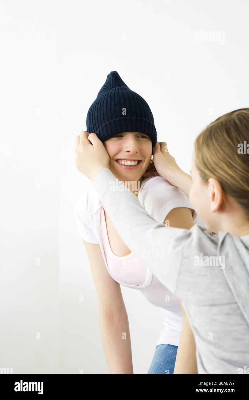 Girl pulling knit hat over her friend's head Stock Photo - Alamy