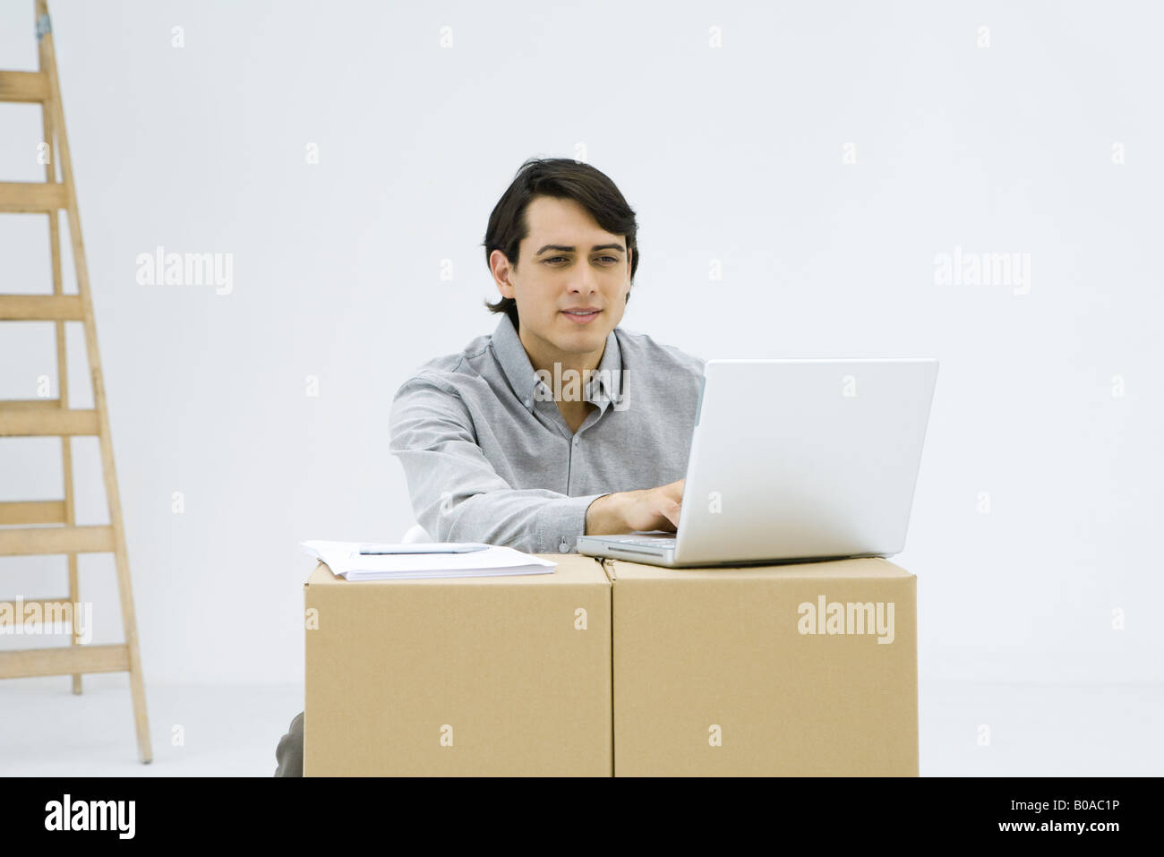 Man working on laptop computer, using cardboard boxes as makeshift desk ...