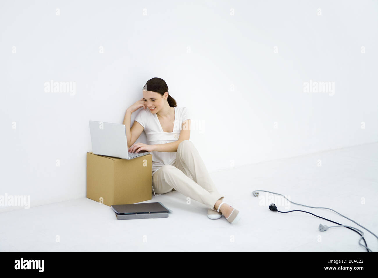 Young woman sitting on the ground, using laptop computer, loose ...