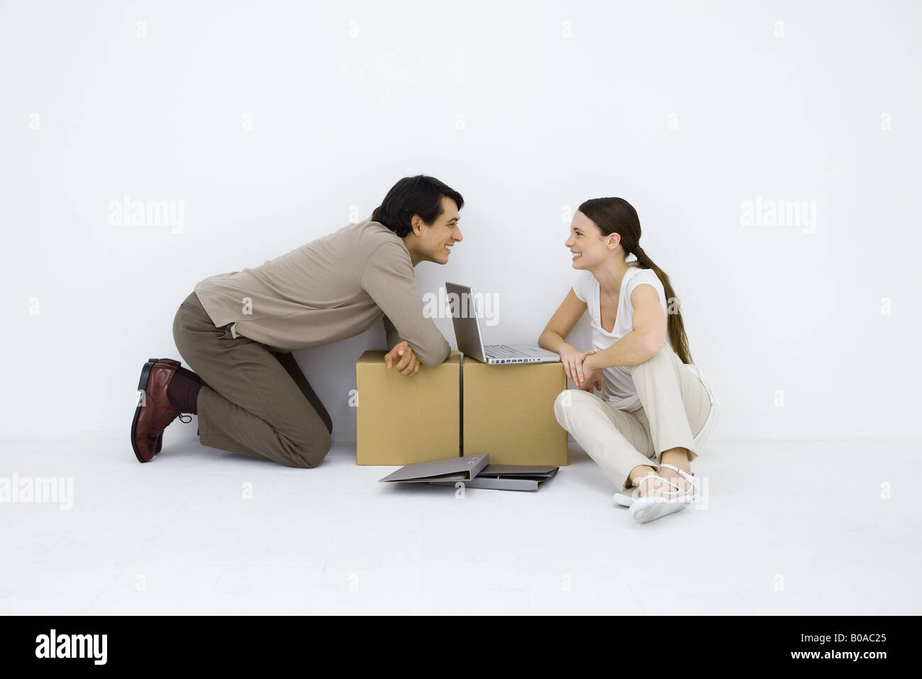 Couple sitting at makeshift desk with laptop computer between them ...