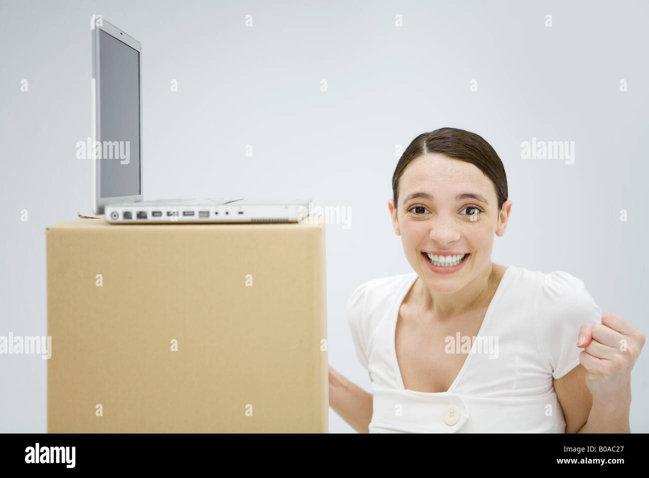 Young woman with laptop computer on top of cardboard box, smiling at ...