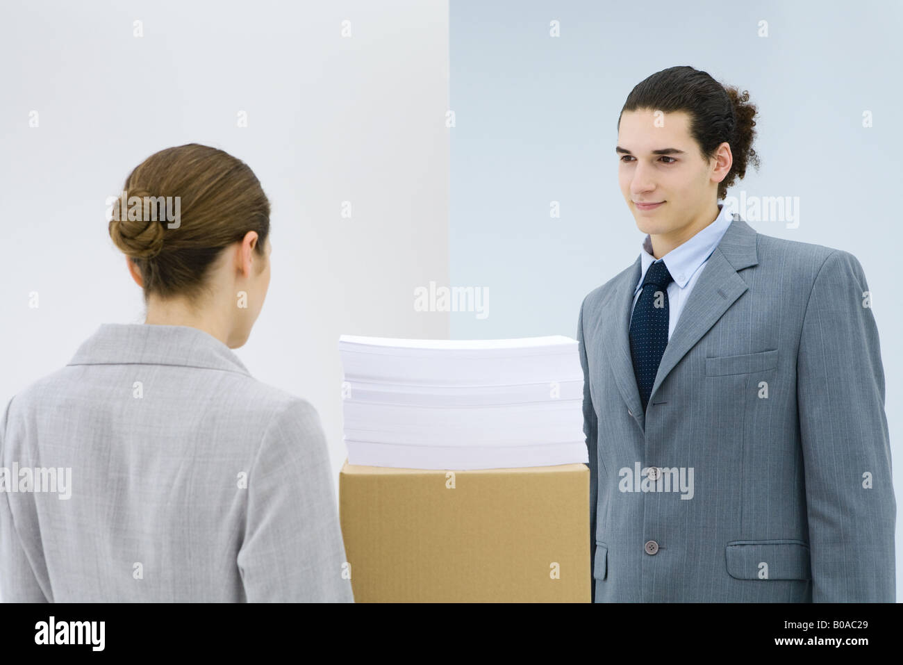 Young professionals standing face to face, documents stacked on ...