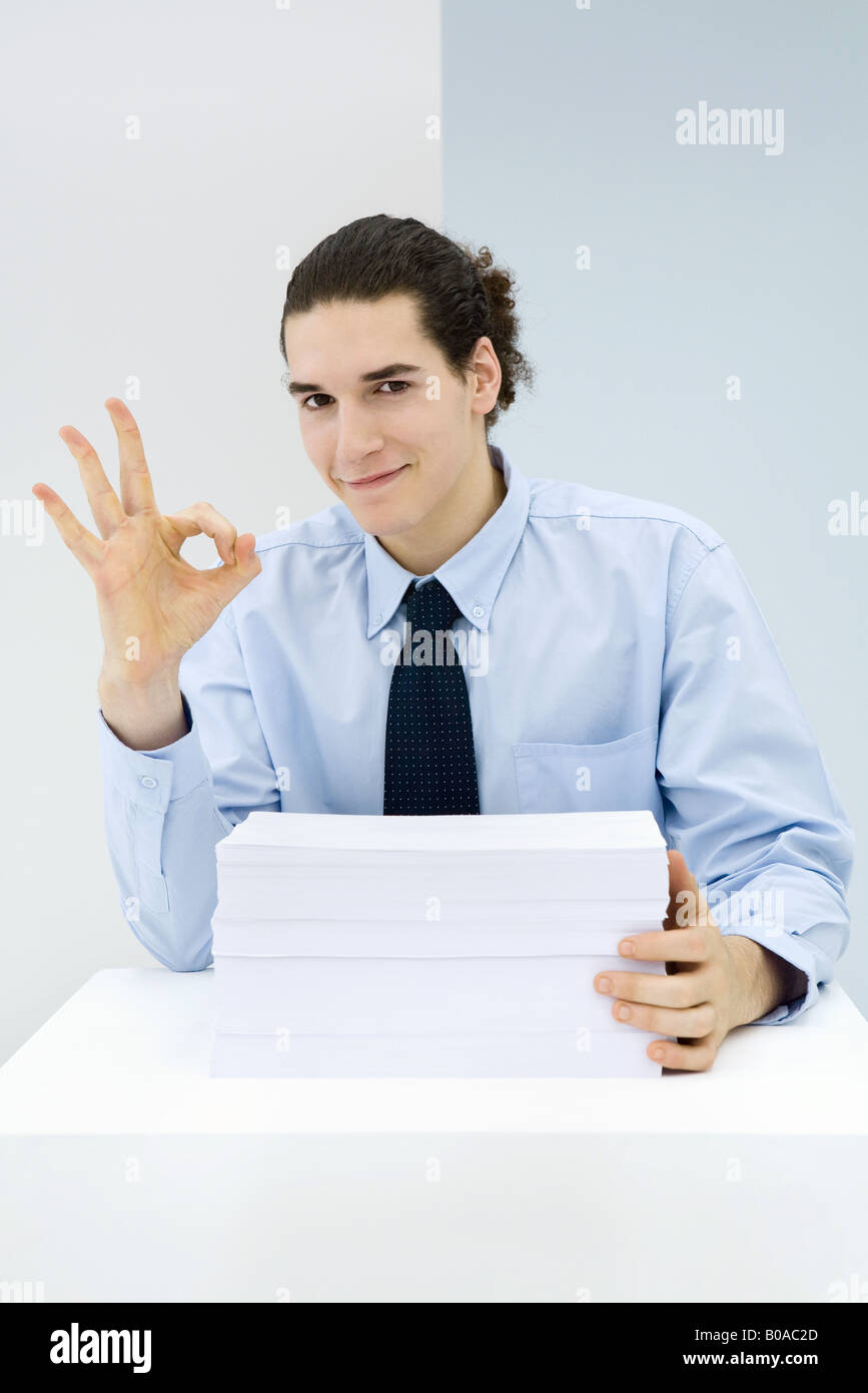 Young professional sitting behind stack of papers, making OK hand ...