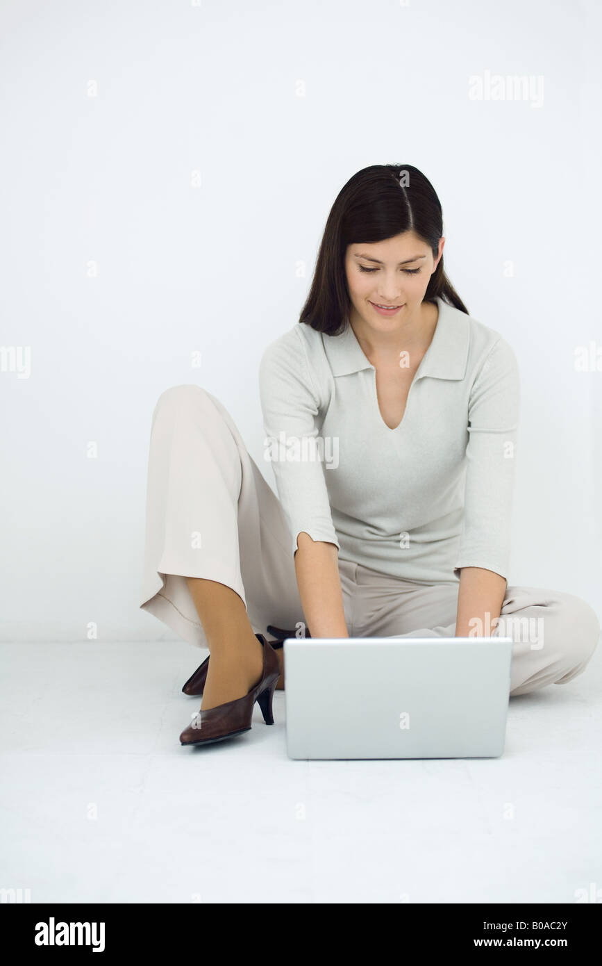 Woman sitting on the ground, using laptop computer, smiling Stock Photo ...