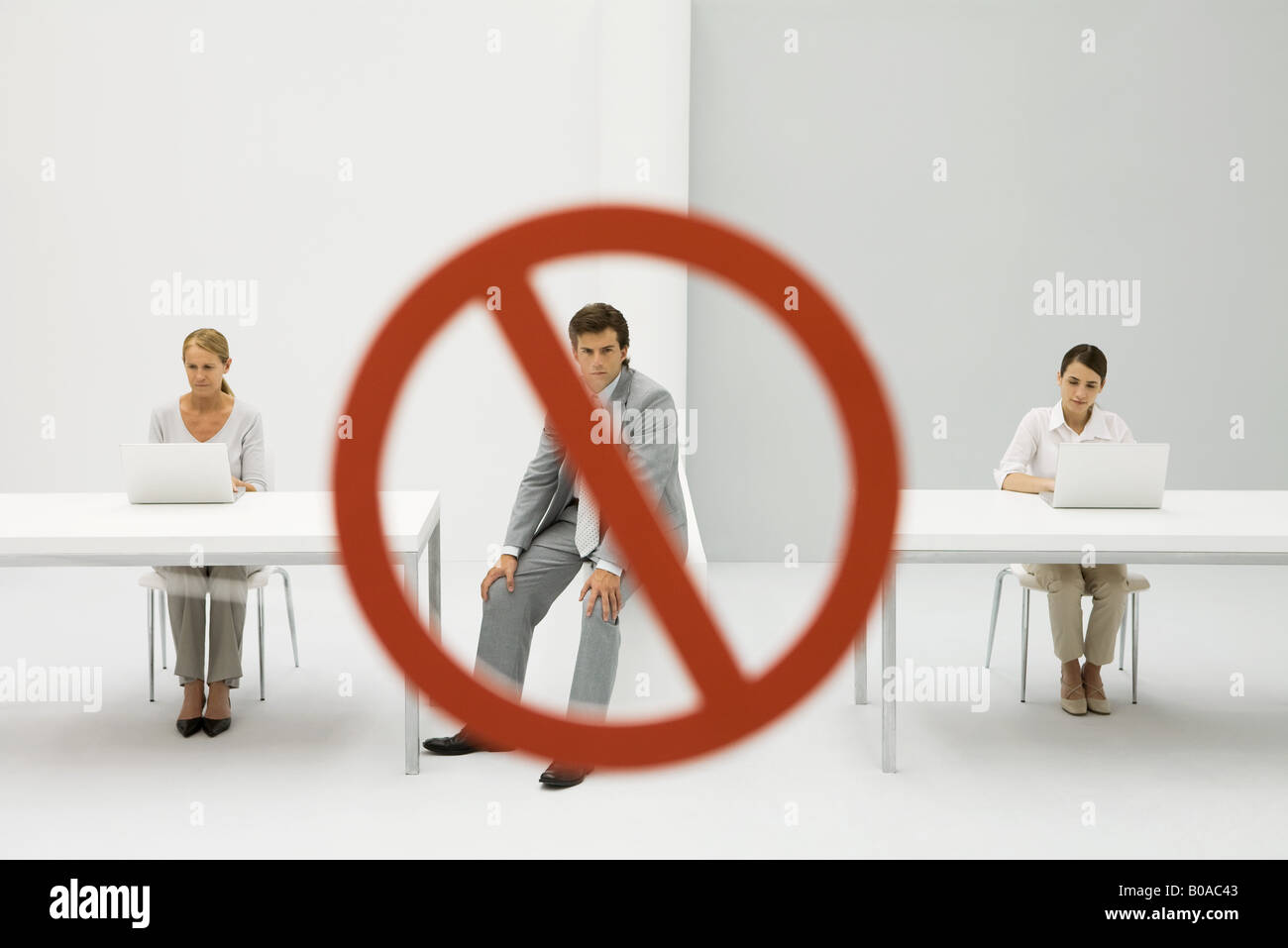 Two women seated in front of laptop computers, warning sign over man ...