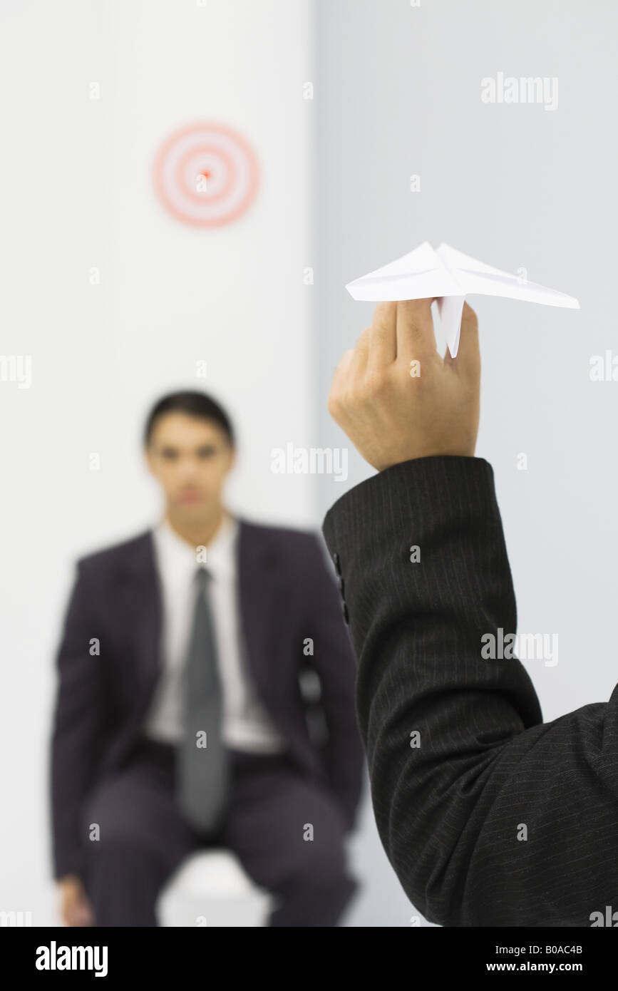 Man holding paper airplane, aiming at target of colleague's head ...