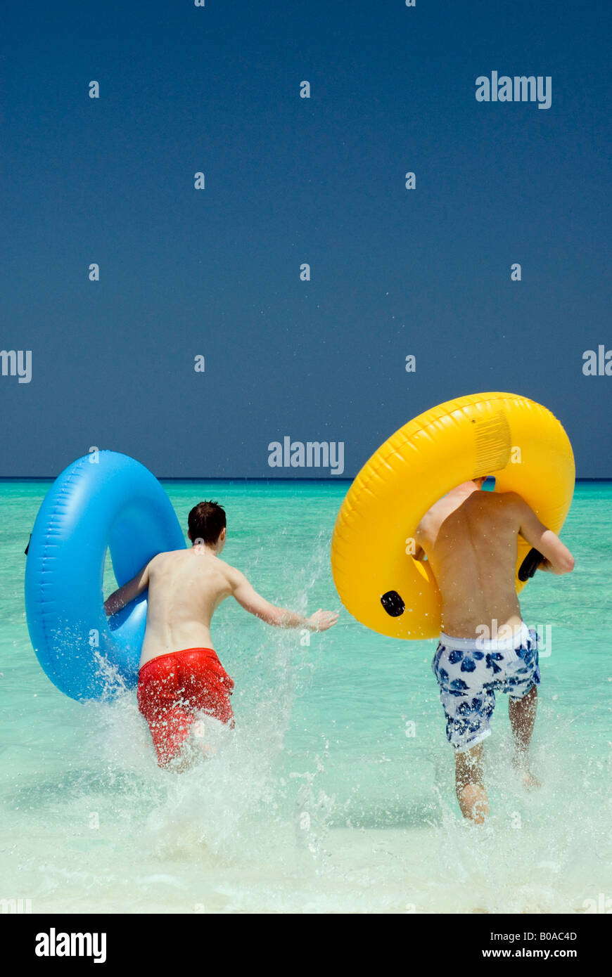 Two teenage boys with inflatable rubber tubes on tropical sandy beach ...