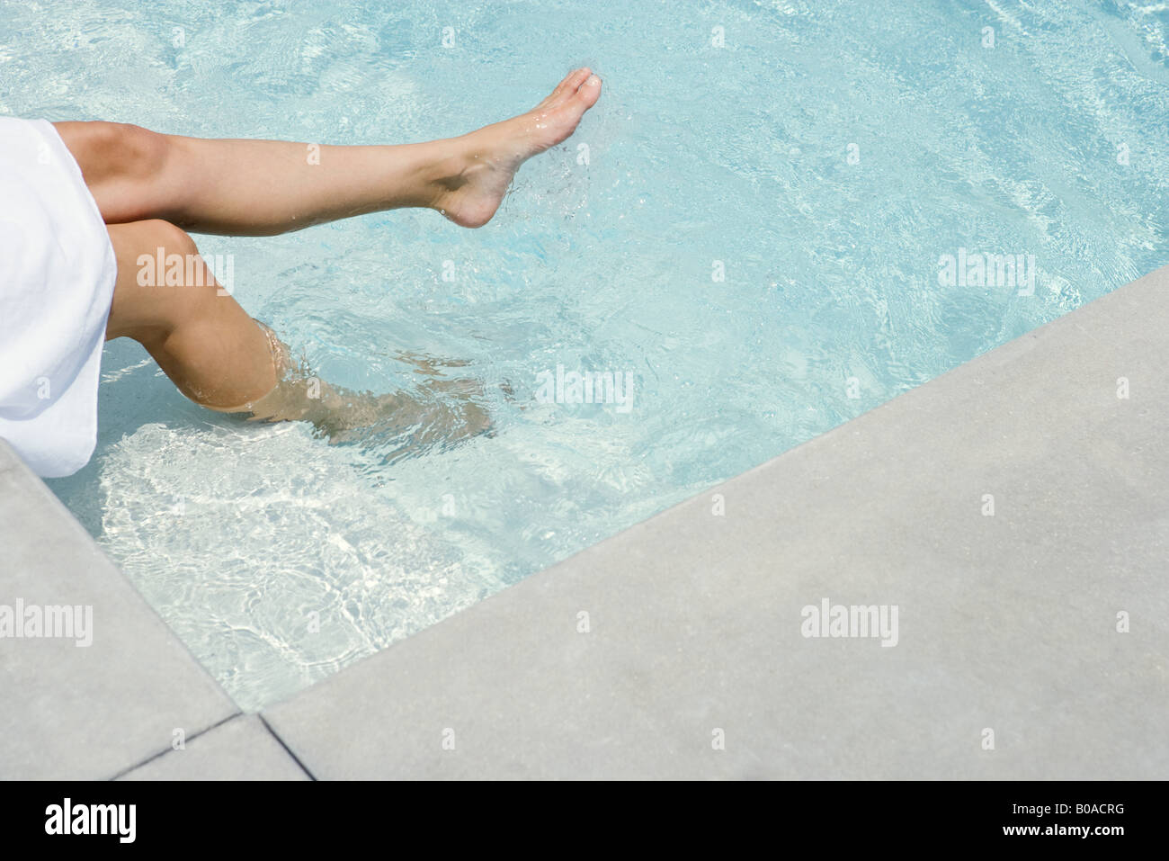 Woman sitting by swimming pool, soaking feet in water, cropped view ...