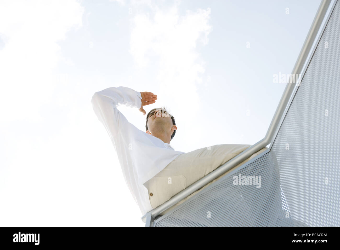 Young man leaning on rail, shading eyes, looking into distance, low ...