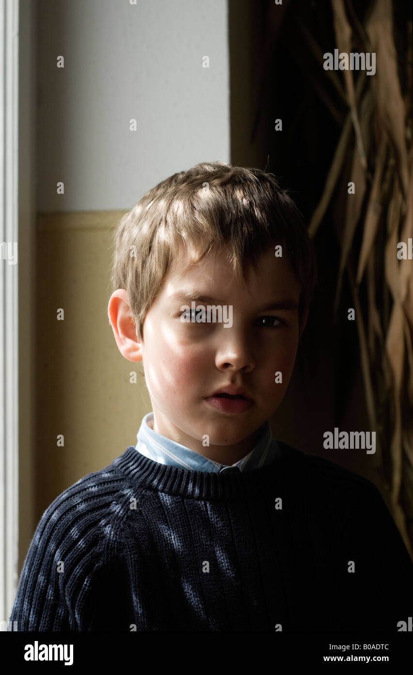 Portrait of a six years old blond german boy standing by the window ...