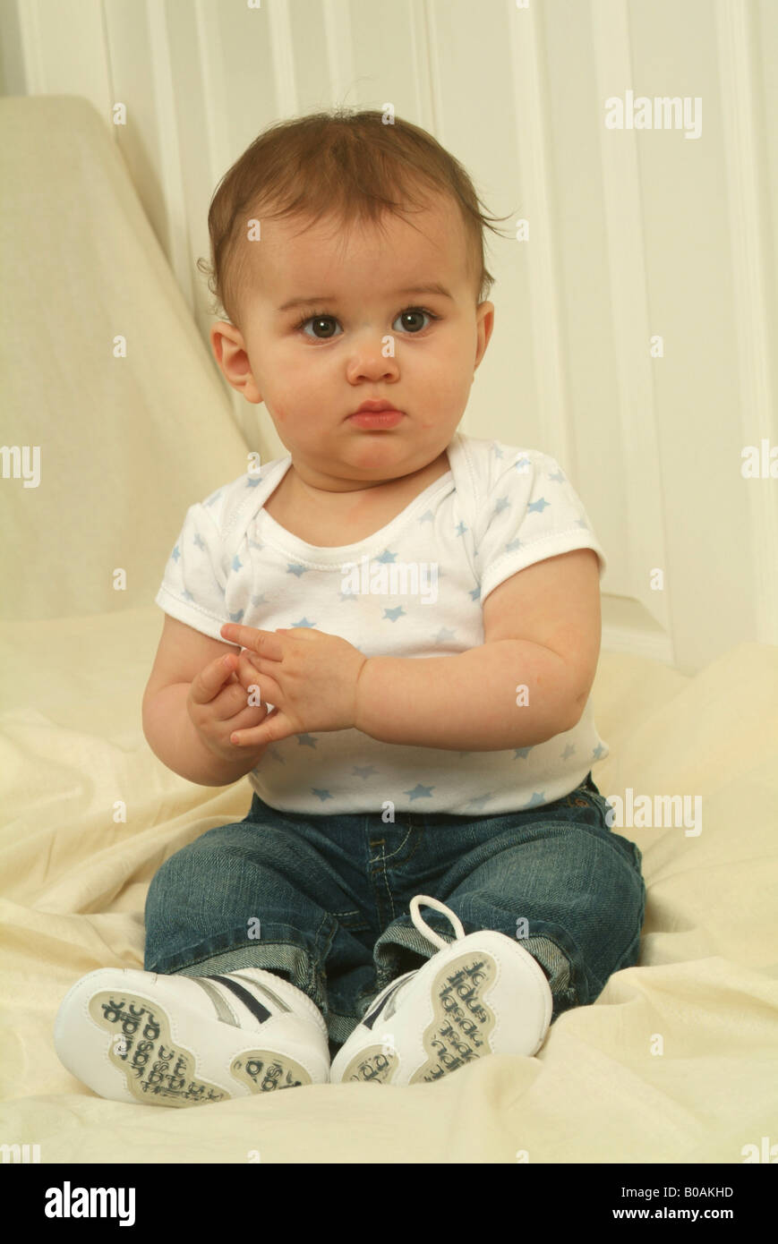 An eight month old baby boy sitting upright on a white couch and ...