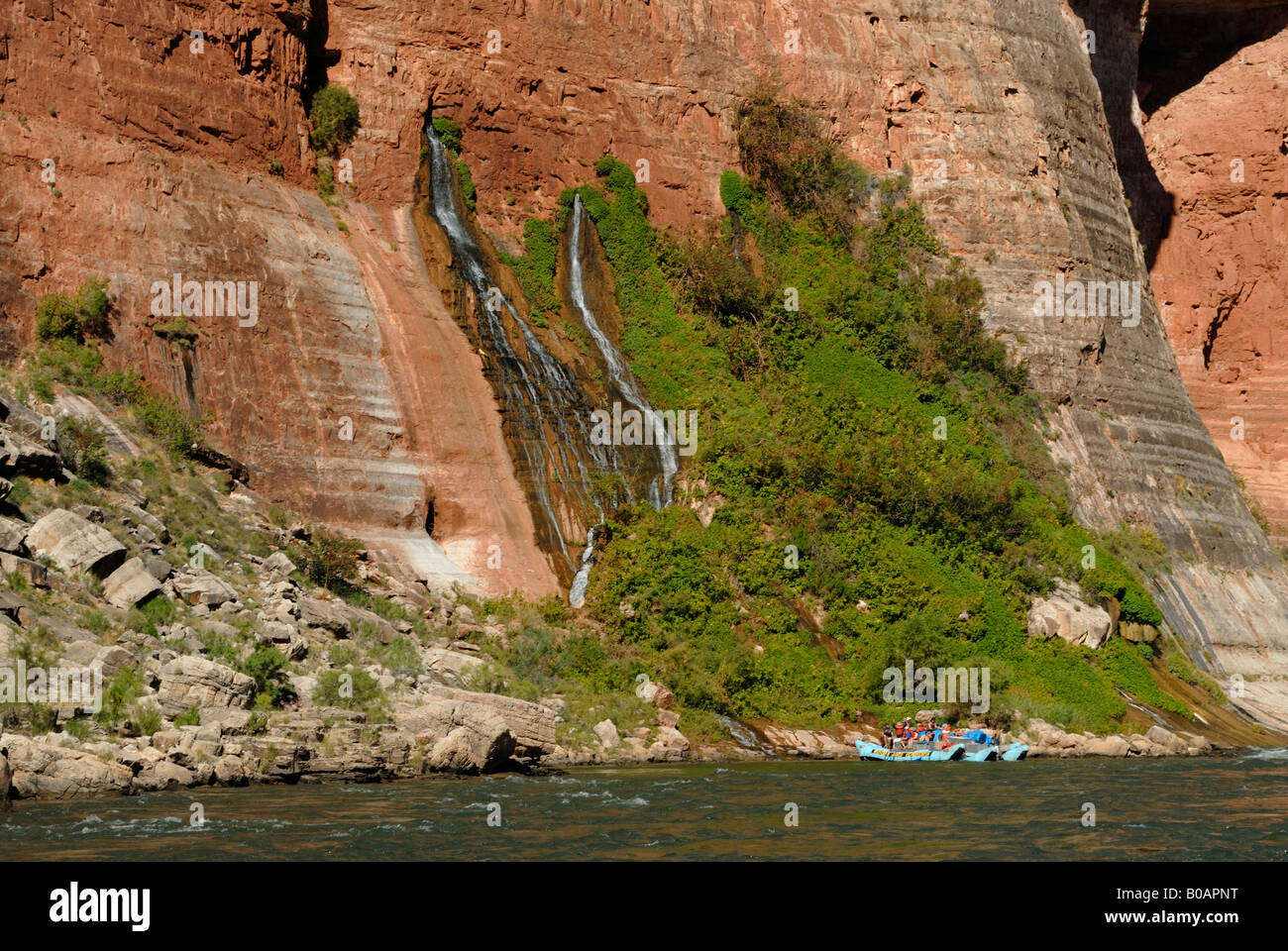 A waterfall coming out from a rock wall below a raft which is rafting ...