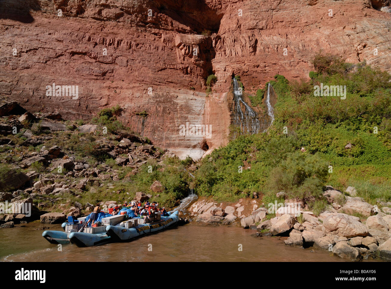 A waterfall coming out from a rock wall below a raft which is rafting ...
