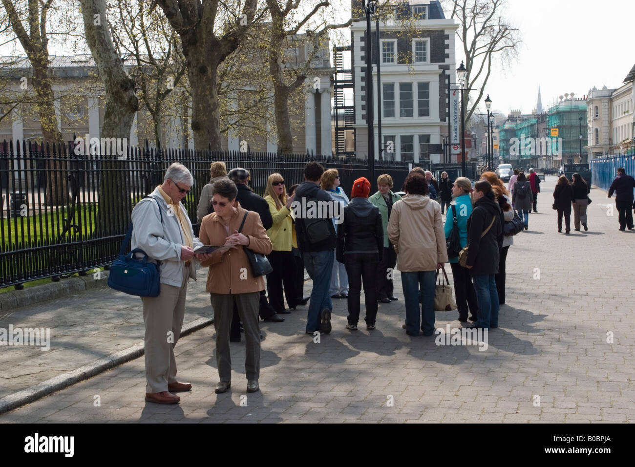 A group of tourists with a tour guide and a couple reading a tourist ...