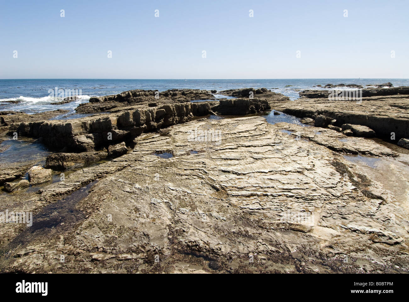 A view of a tidepool at low tide exposes a sharp reef covered with ...