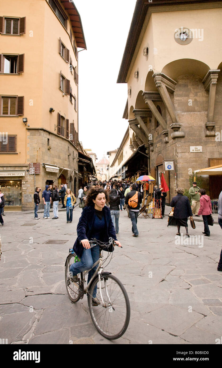 a young female cyclist on the street in front of Ponte Vecchio Bridge ...