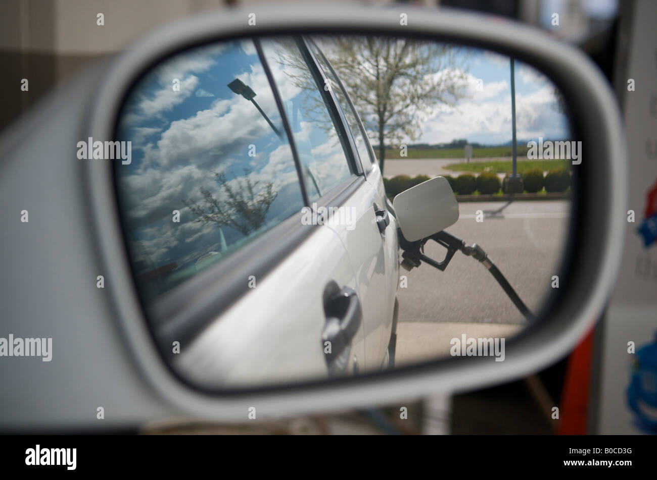 View in a side view mirror of a gas pump fueling a white vehicle at a ...