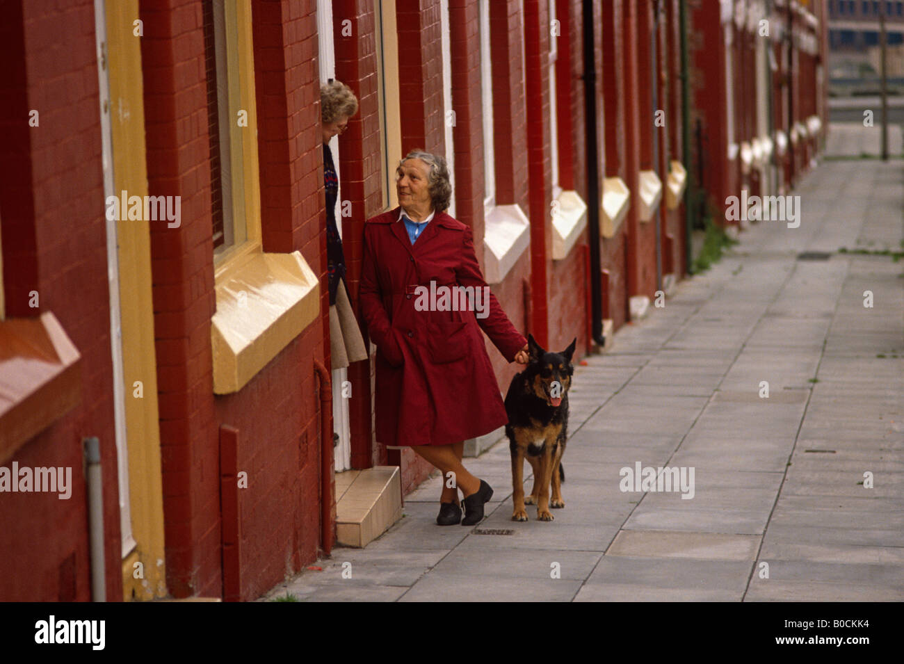 Old neighbours stand gossiping outside red painted house in empty ...